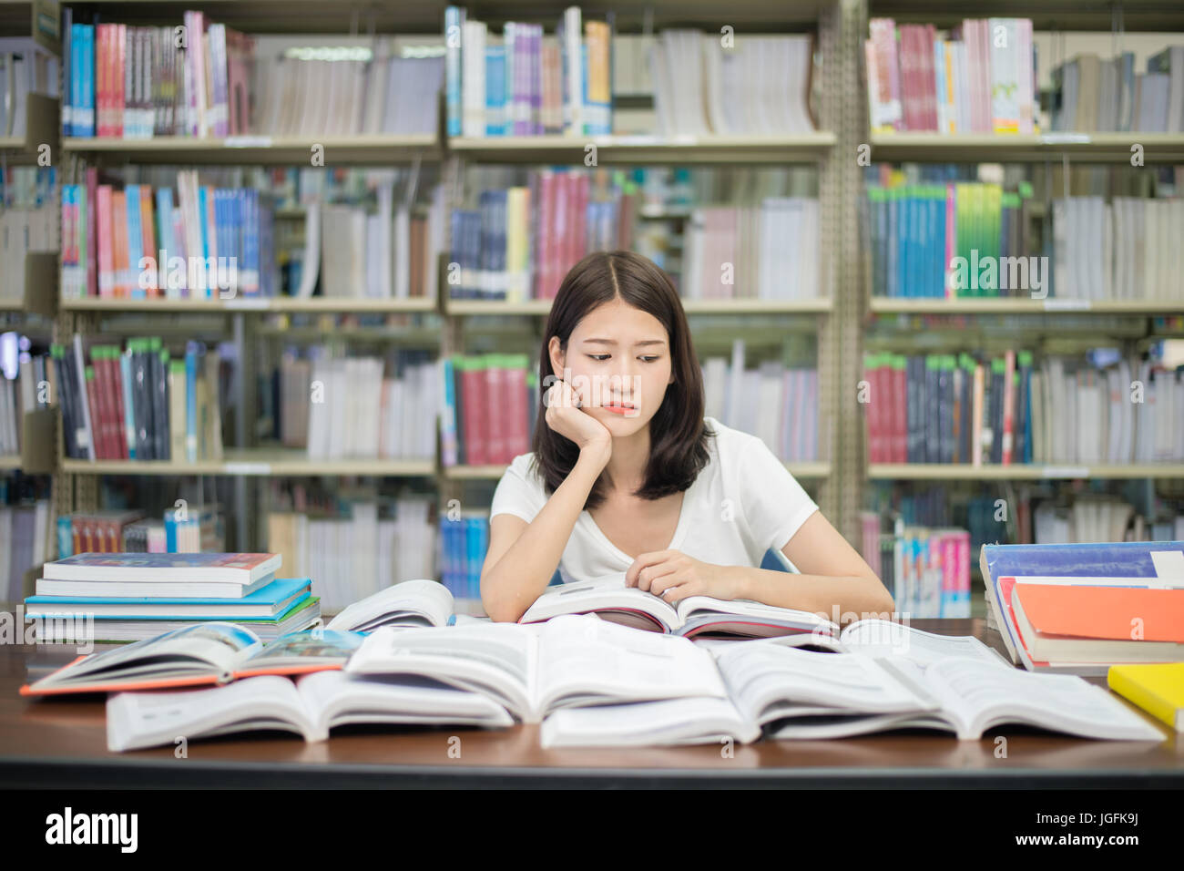 Asian woman student boring reading book at library with a lot of books ...