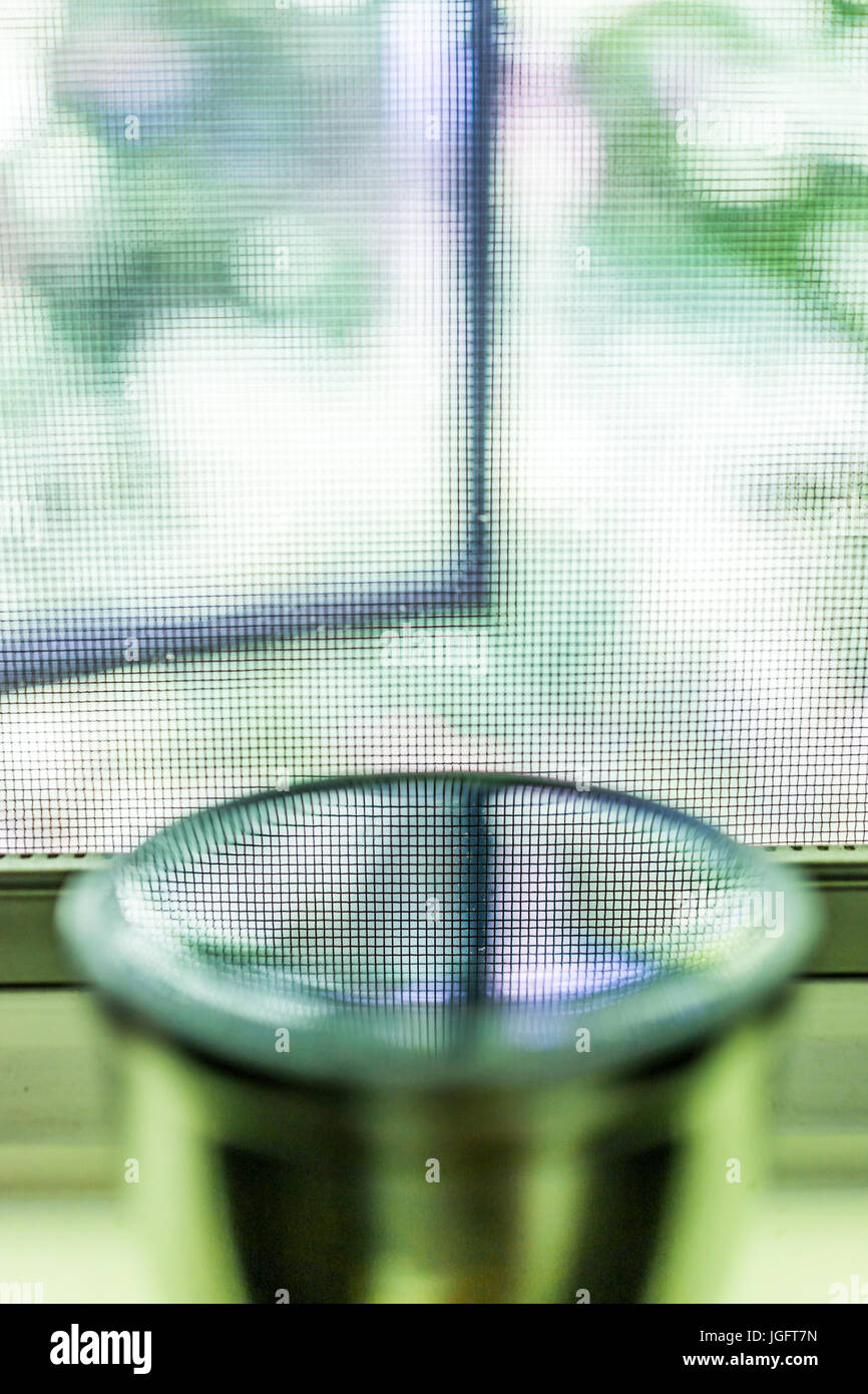 Reflection of mesh window and green foliage in cup of water or tea on ...