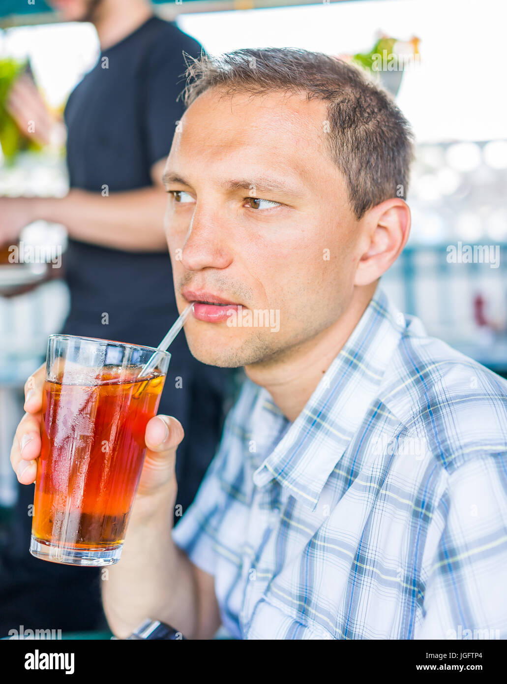 Portrait of young man drinking iced tea or alcoholic beverage with ...