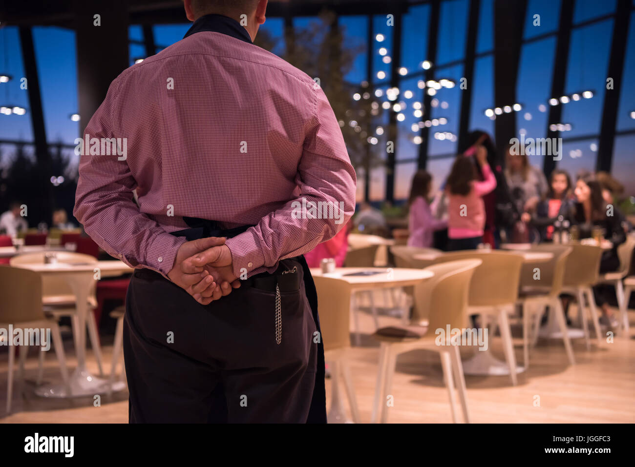 Rear view of young confident waiter standing with hands behind his back ...