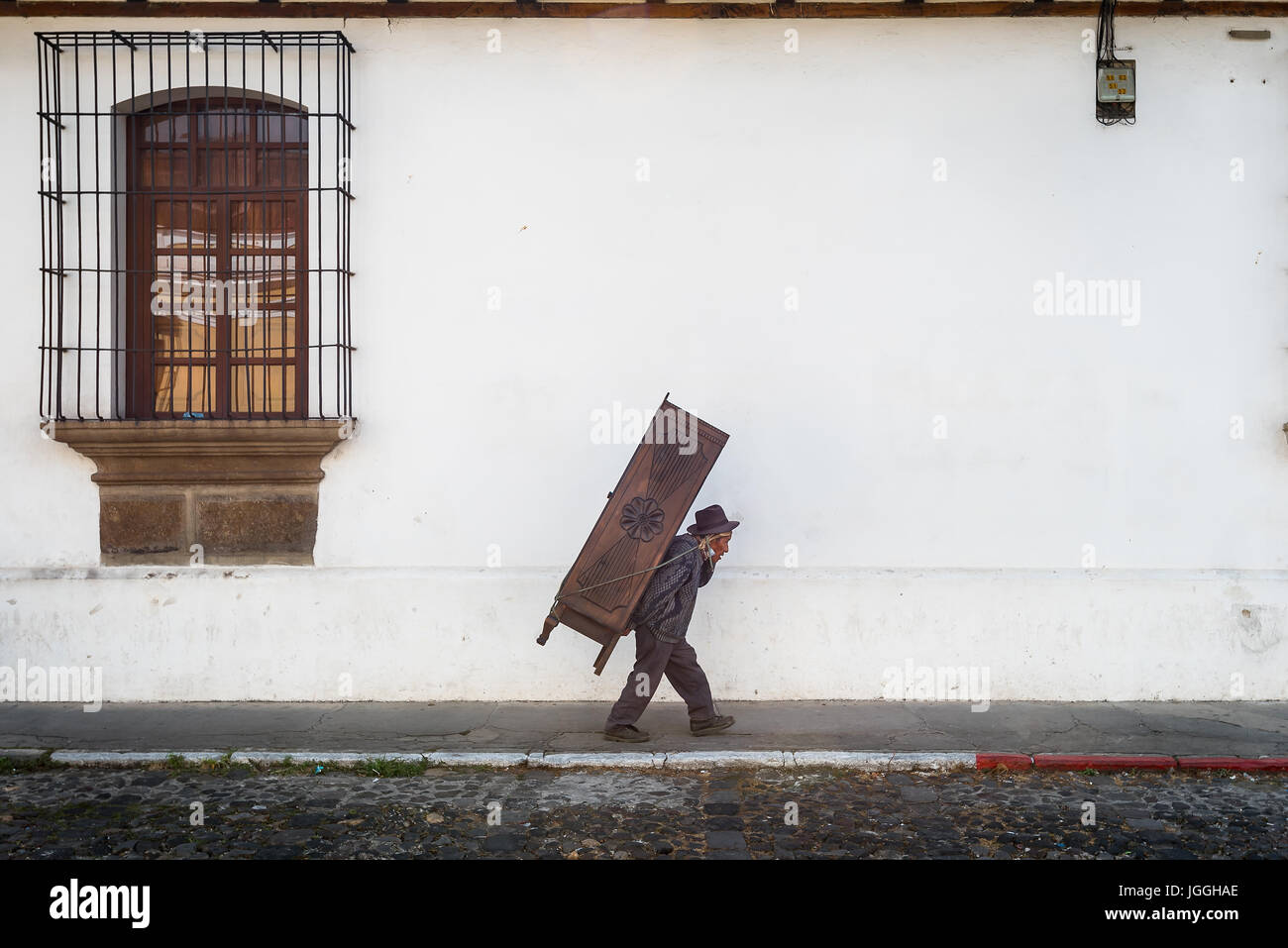 A poor Mayan man in ragged traditional clothes carries a heavy load ...