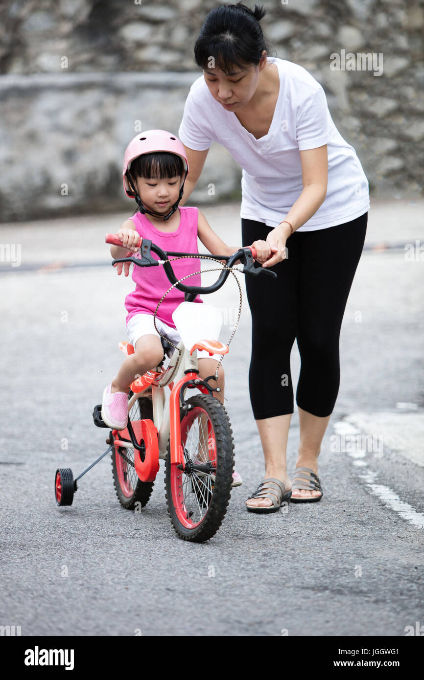 Asian Chinese little girl riding bicycle with mom guide on tar road ...