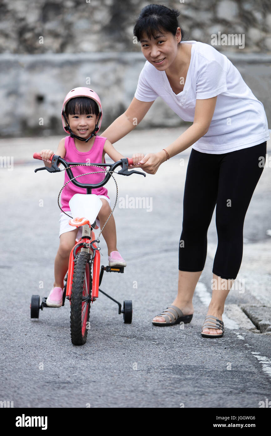 Asian Chinese little girl riding bicycle with mom guide on tar road ...