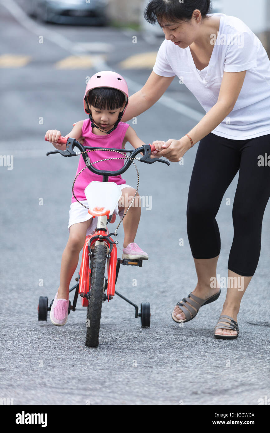 Asian Chinese little girl riding bicycle with mom guide on tar road ...
