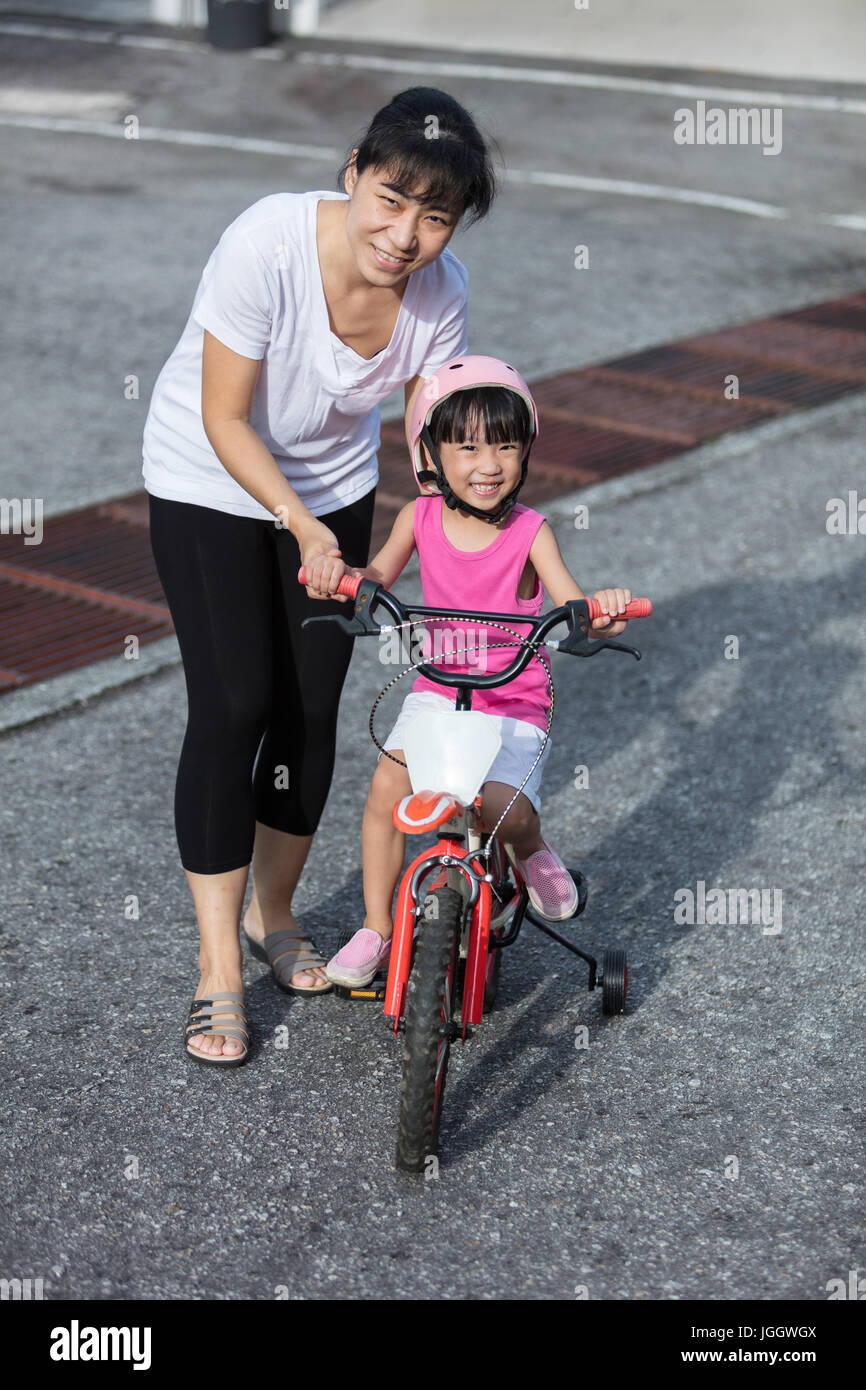 Asian Chinese little girl riding bicycle with mom guide on tar road ...