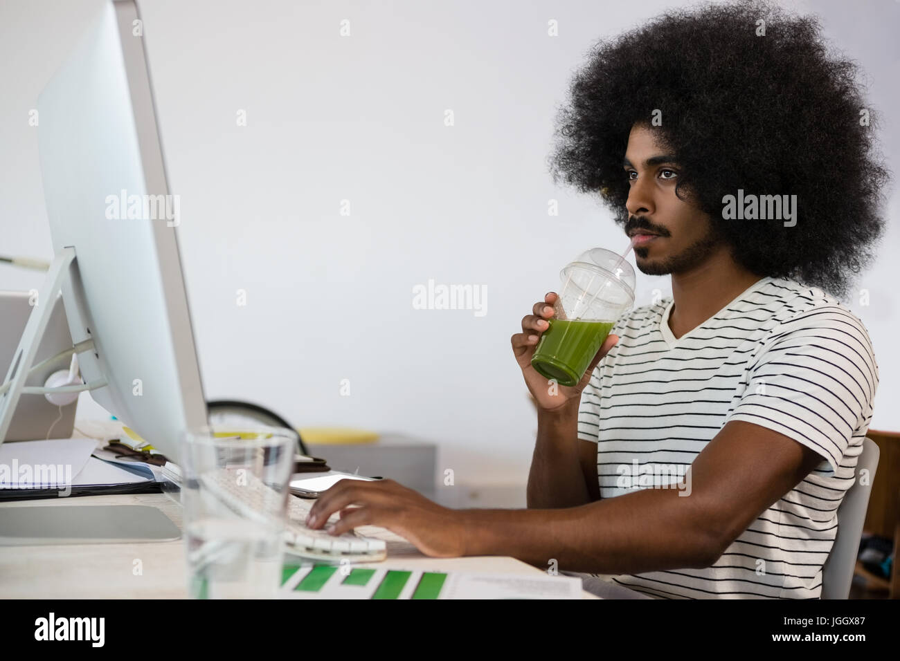 Young man having drink while using computer at desk in office Stock ...