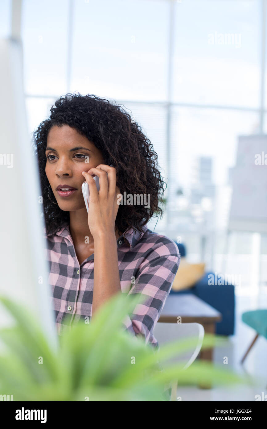 Female executive talking on mobile phone while working on computer at ...