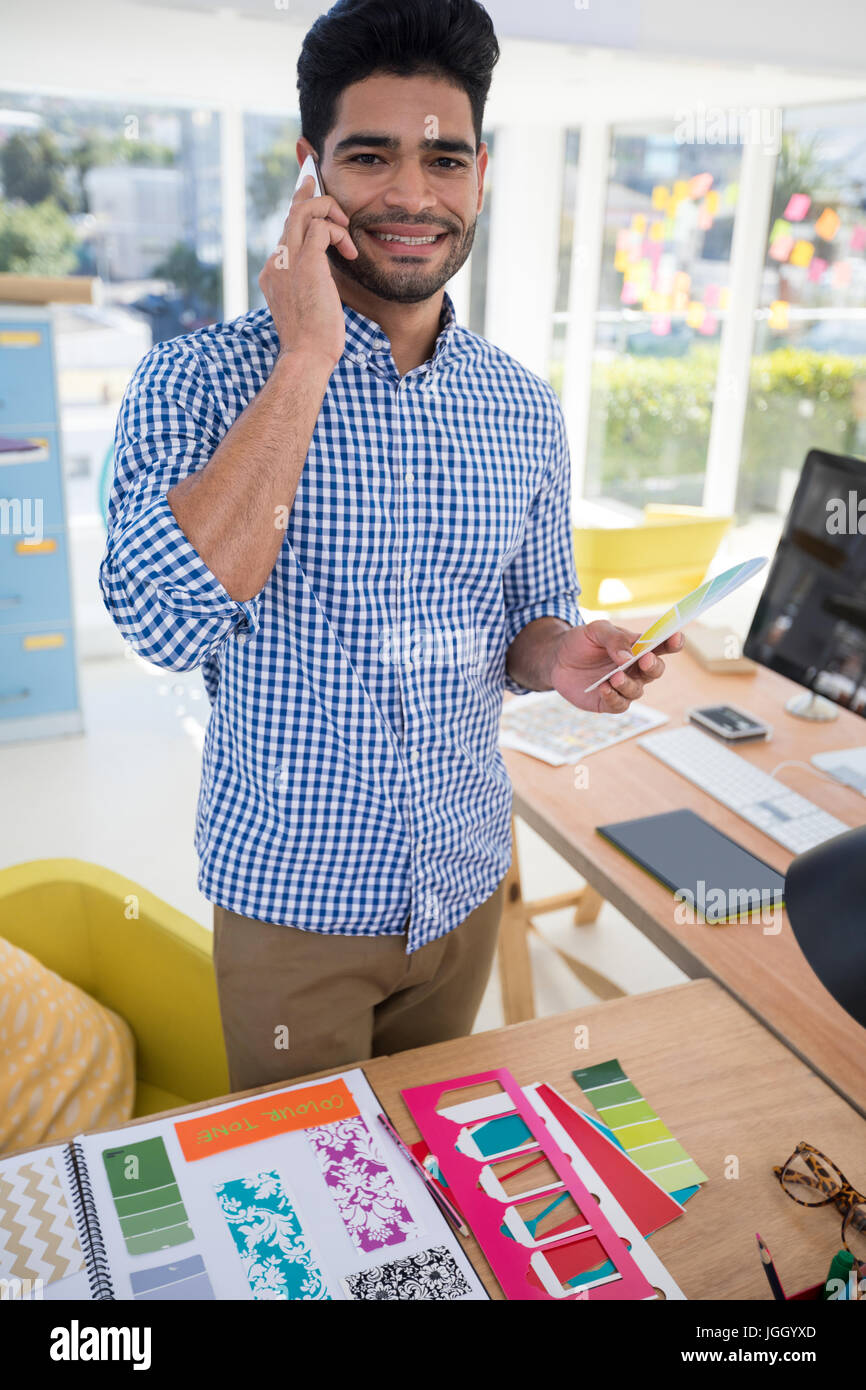 Male graphic designer talking on mobile phone at desk in the office ...
