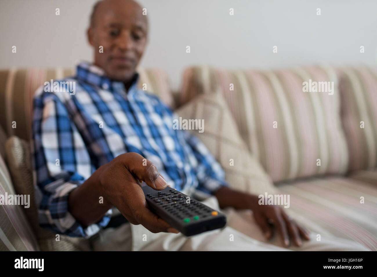 Man holding remote control while sitting on sofa in living room at home ...