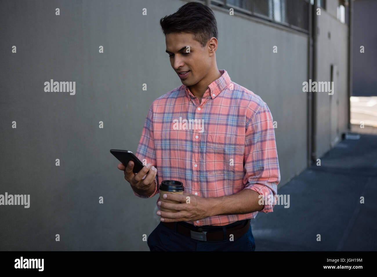 Smiling young man using mobile phone while walking by wall Stock Photo ...