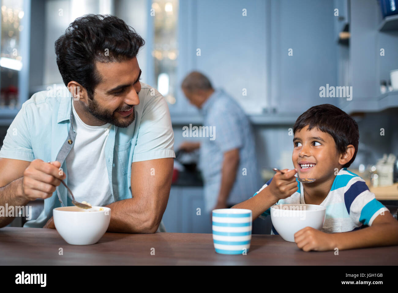 Father and son having breakfast at table with man in background Stock ...
