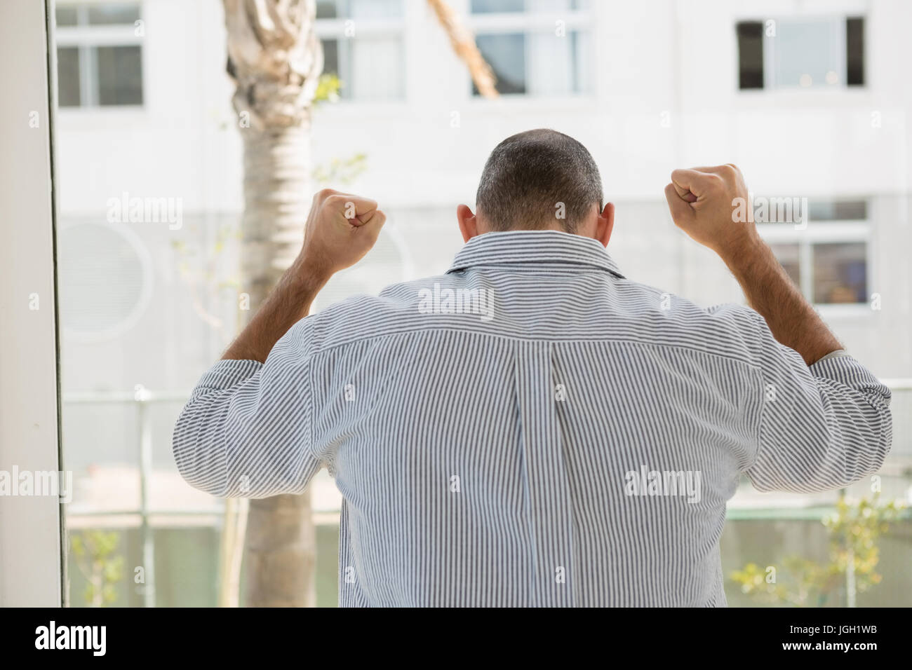 Rear view of frustrated designer standing by glass window at office ...