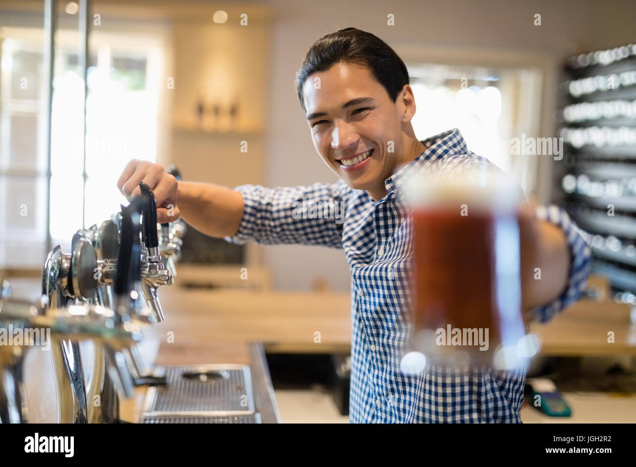 Portrait of bar tender offering glass of beer to customer at bar ...