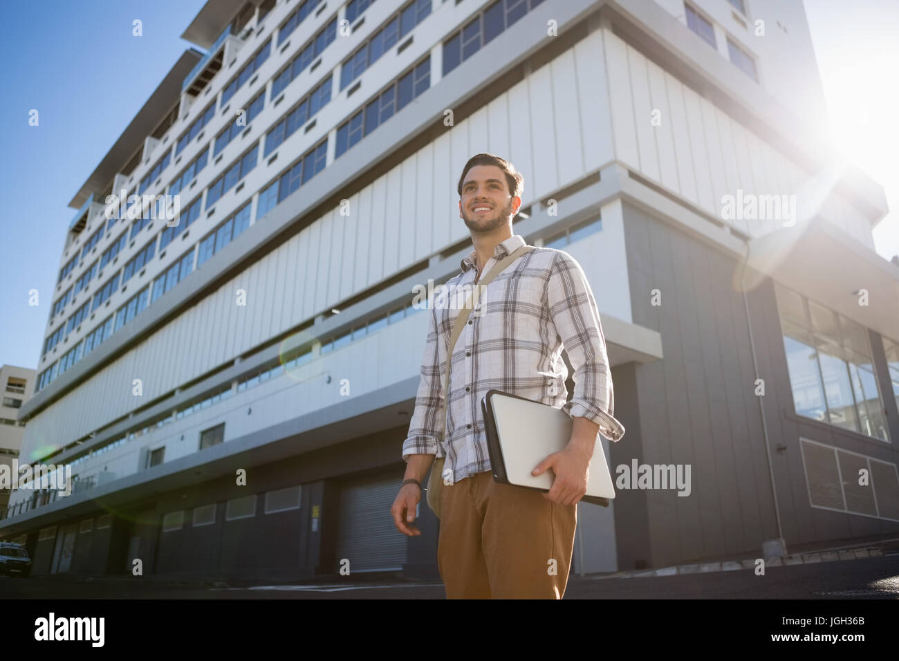 Smiling thoughtful man looking away while standing against building in ...