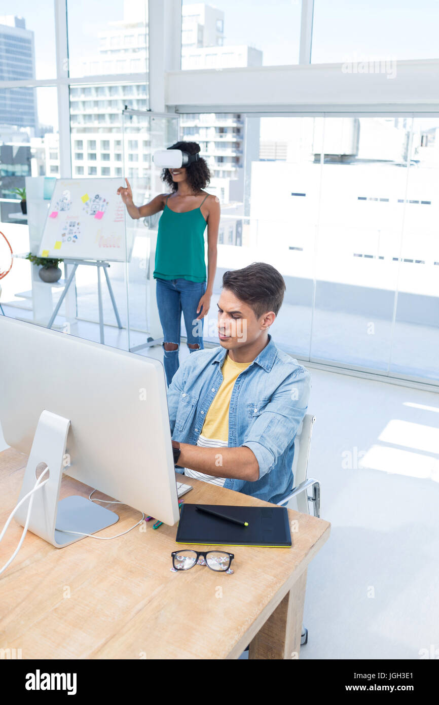 Male executive working on computer while female executive using virtual ...