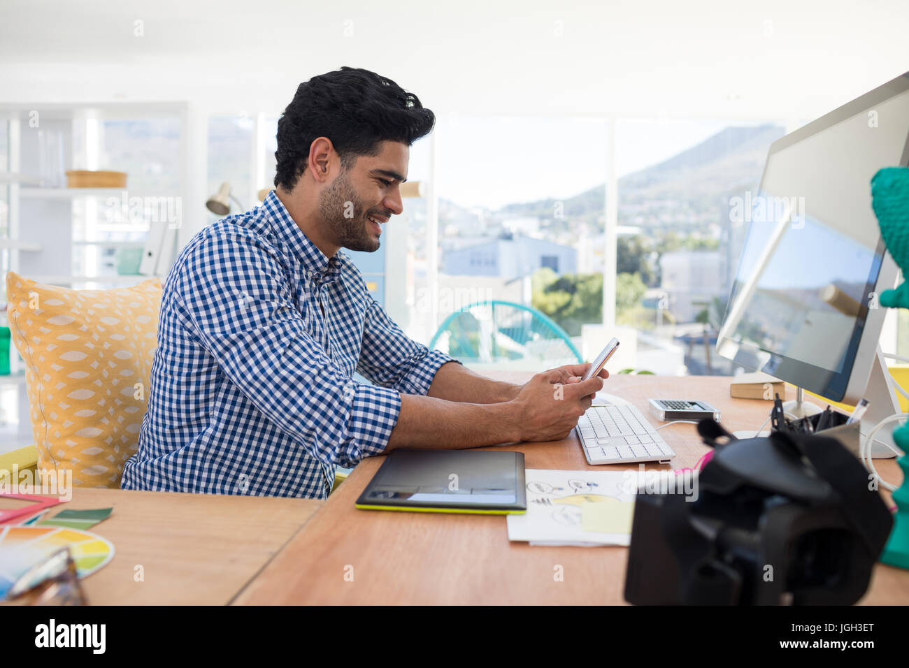 Graphic designer using mobile phone at desk in the office Stock Photo ...