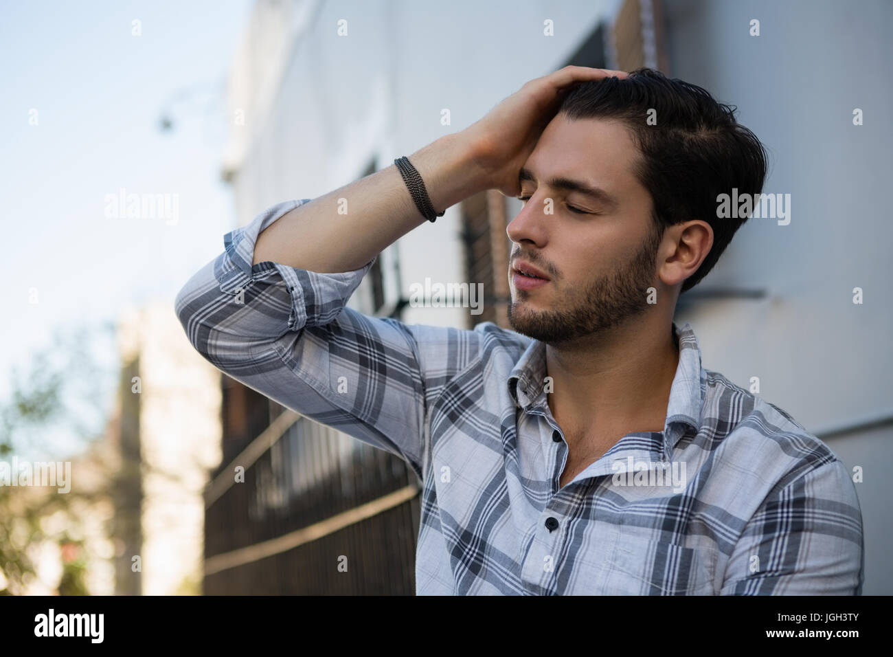 Tensed man with eyes closed sitting by wall Stock Photo - Alamy
