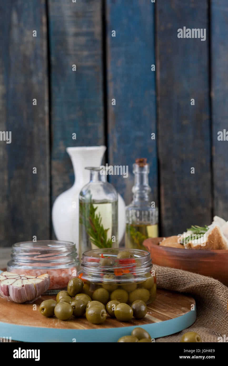 Olives in container by herbs with oil bottle on table against wooden ...