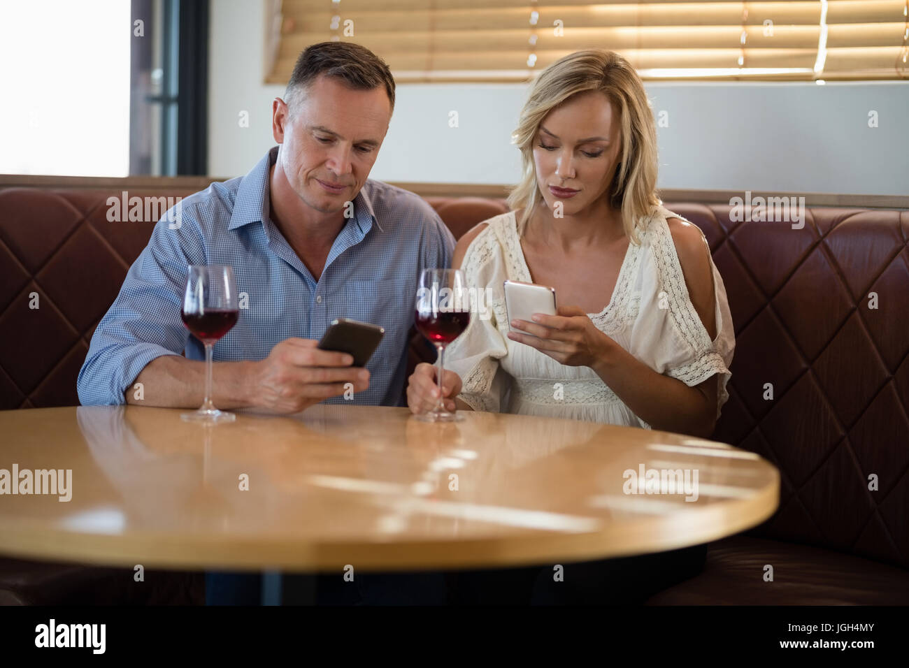 Couple using mobile phones while having glass of wine in restaurant ...