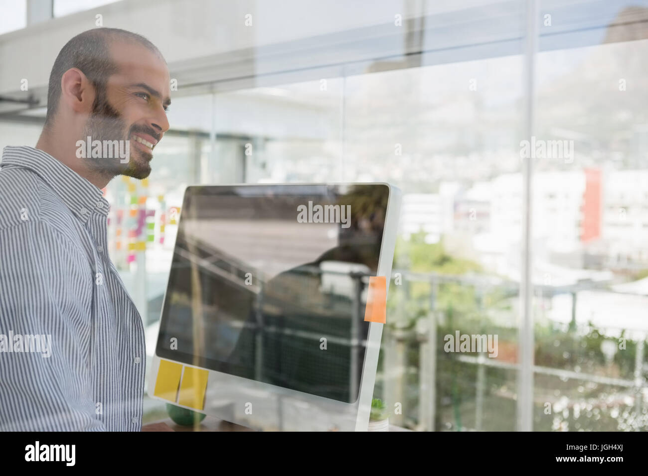 Smiling designer looking away while standing by computer seen through ...