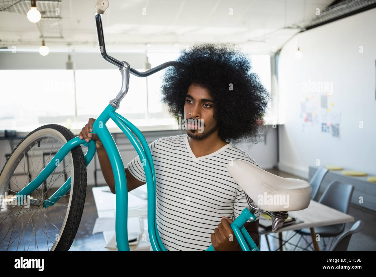 Young man with curly hair holding bicycle at creative office Stock ...