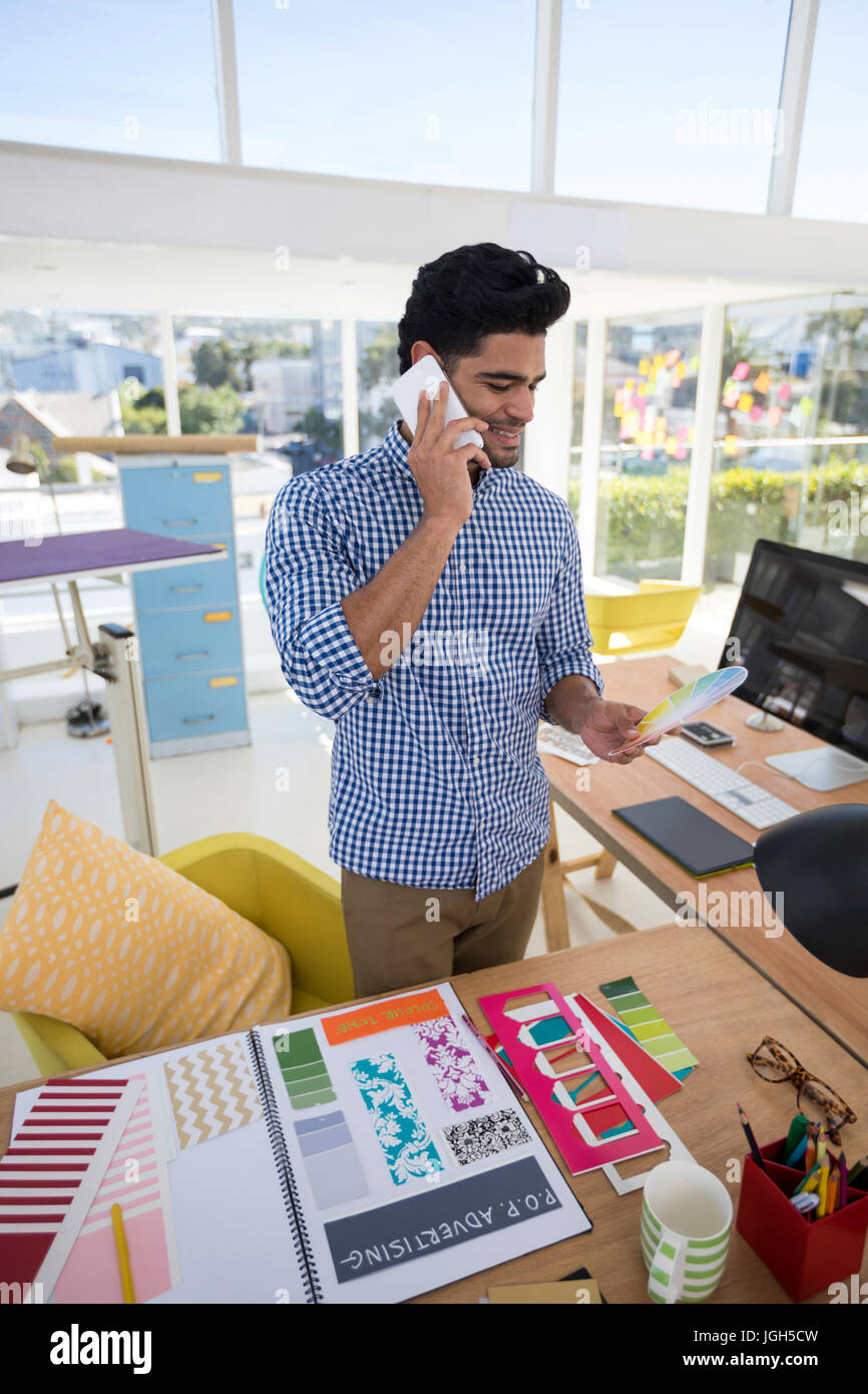 Male graphic designer talking on mobile phone at desk in the office ...
