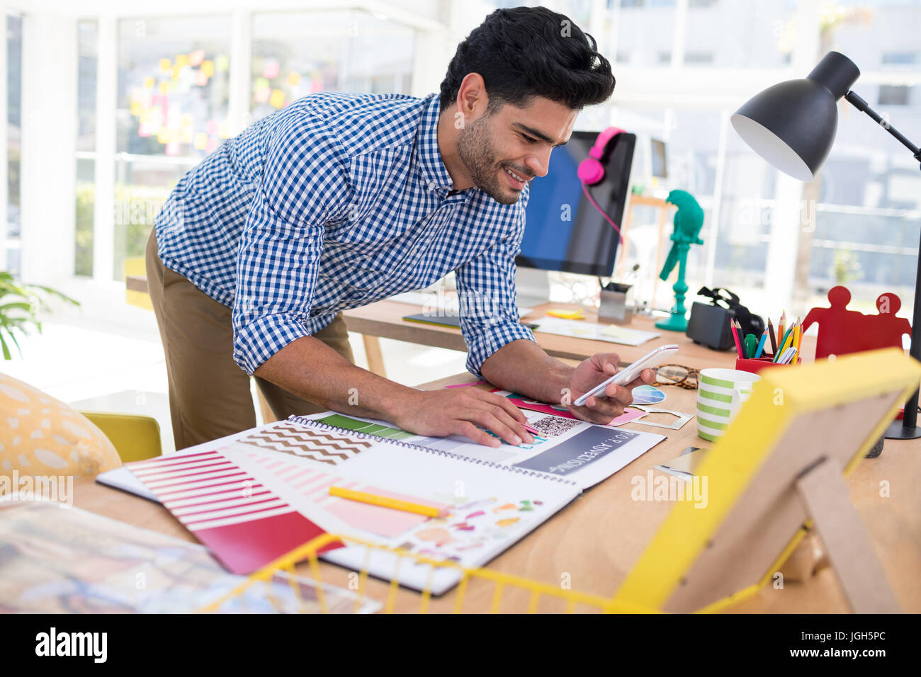 Male graphic designer using mobile phone while working at desk in the ...