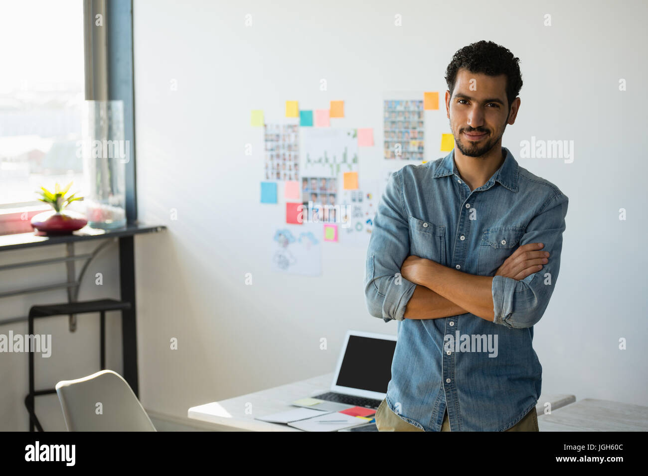 Portrait of confident young businessman standing against wall at office ...