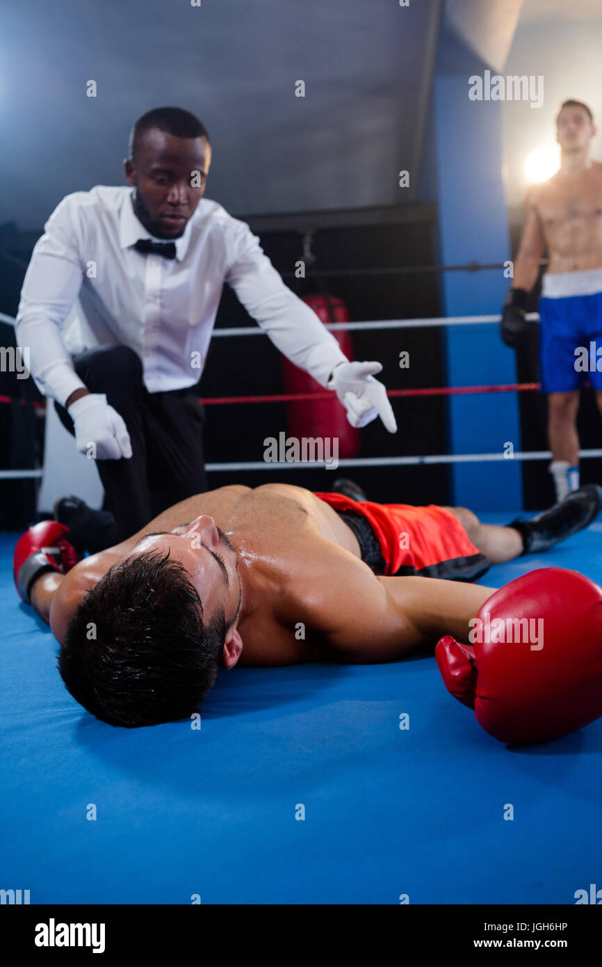 Male boxer looking while referee counting by athlete in boxing ring ...