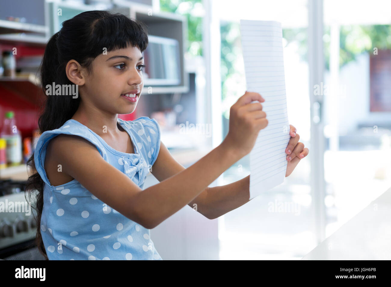 Girl reading paper in kitchen against window Stock Photo - Alamy