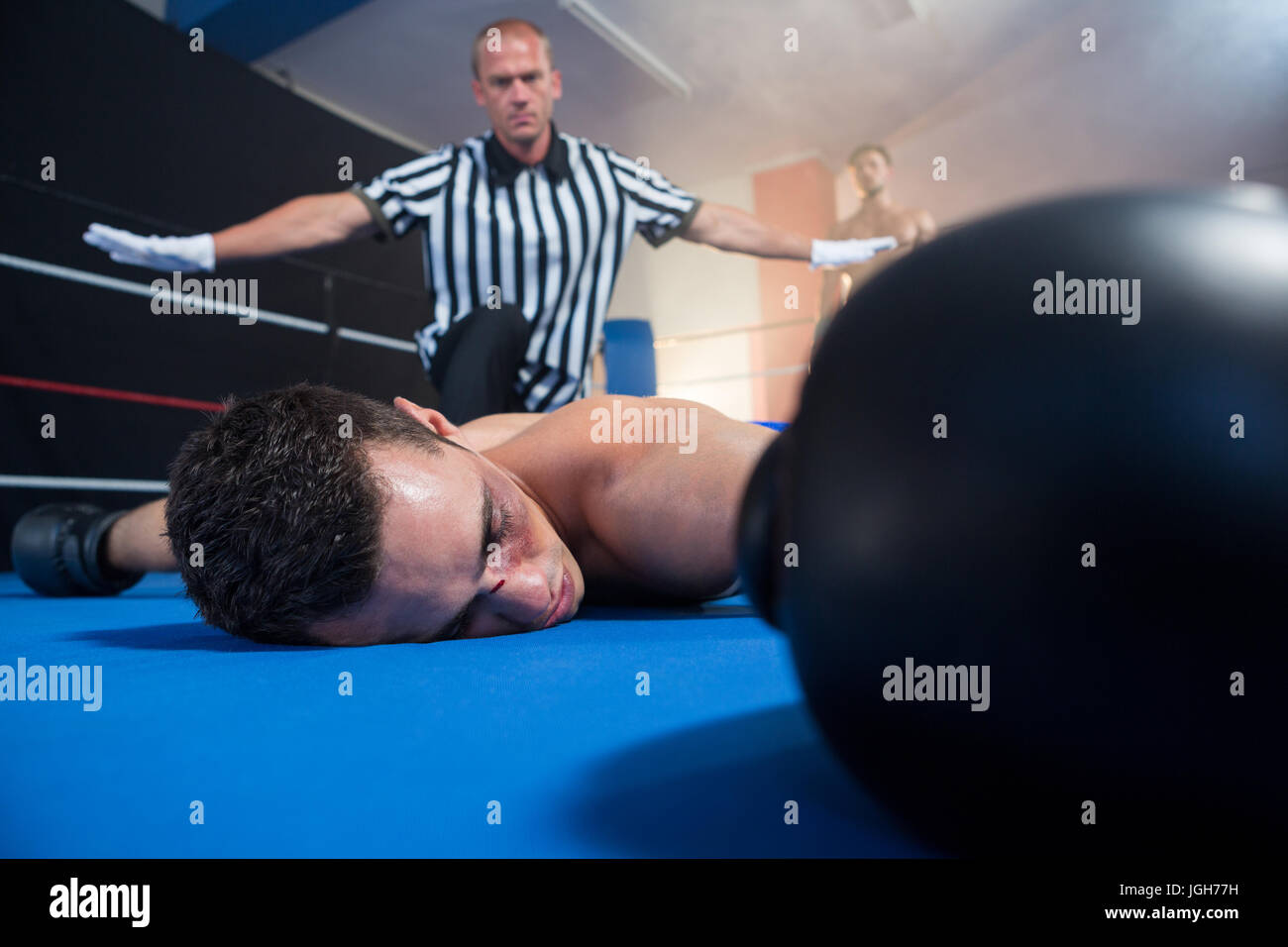 Referee gesturing with arms outstretched by unconscious male boxer ...
