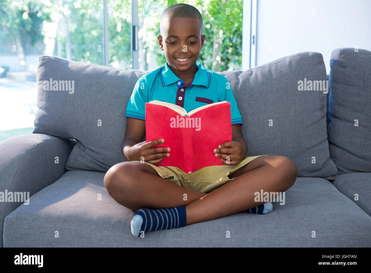Smiling boy reading novel sitting on sofa in living room at home Stock ...