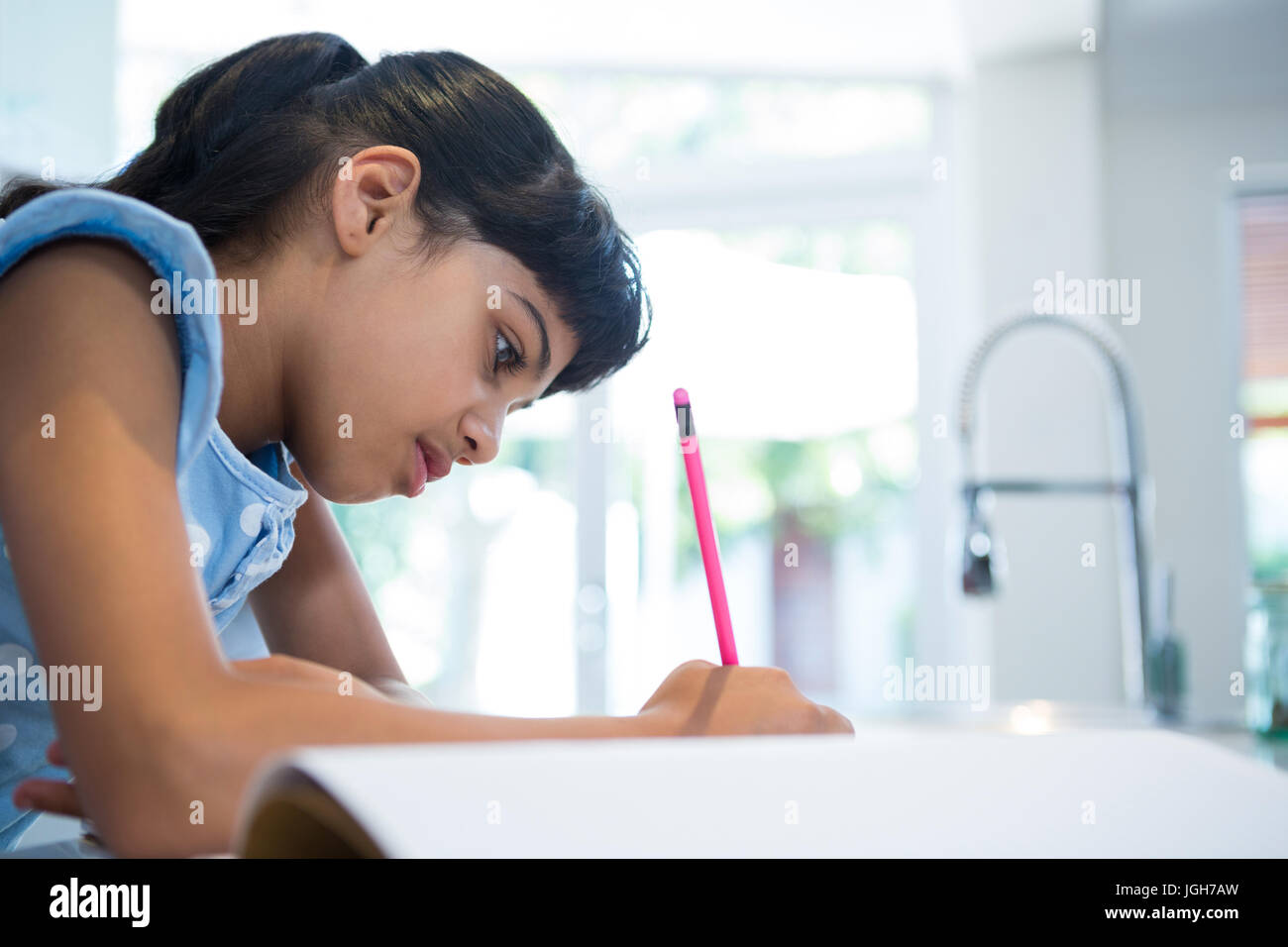 Side view of girl writing in book against window Stock Photo - Alamy