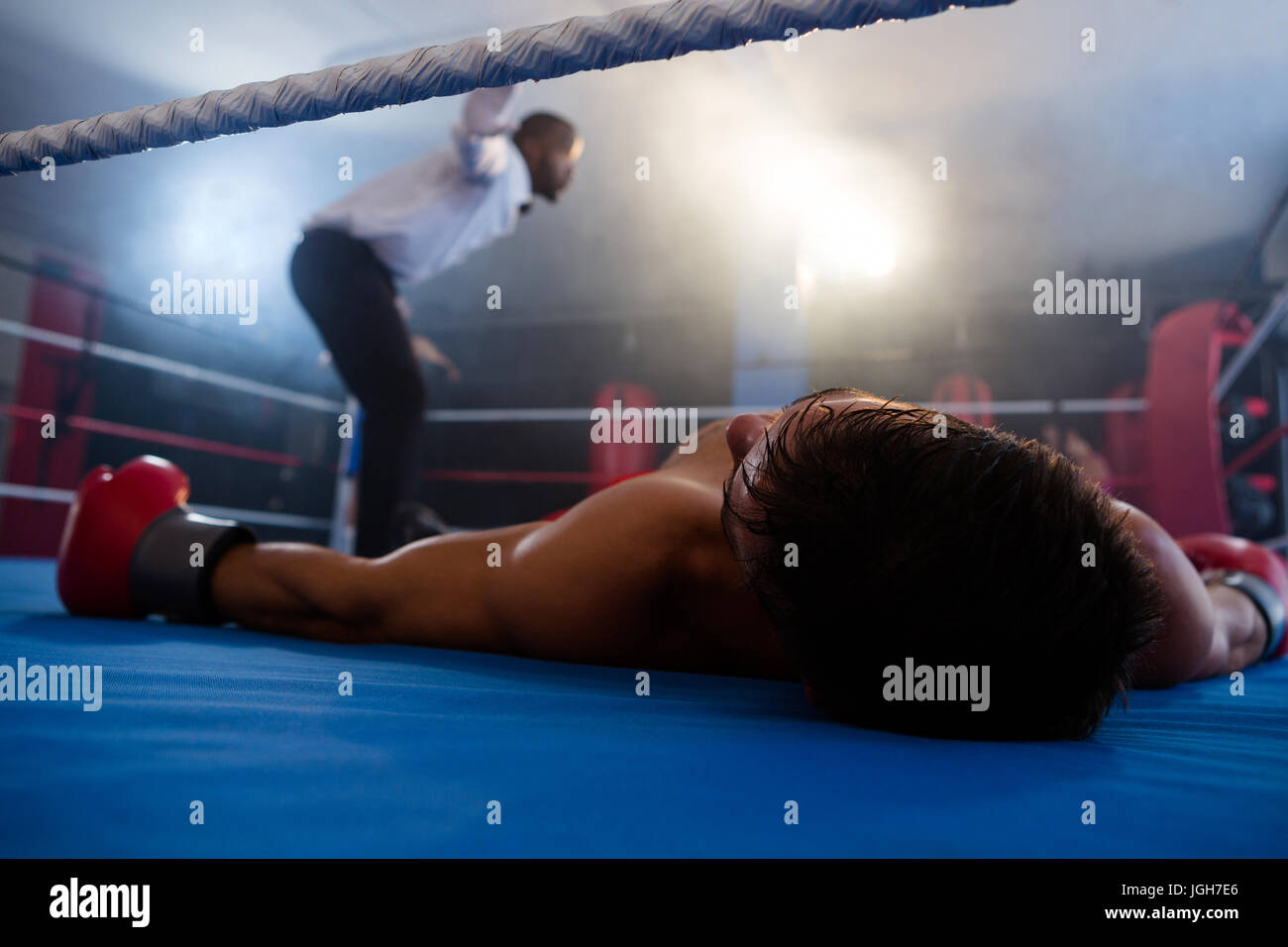 Unconscious male boxer lying by referee in boxing ring at fitness ...