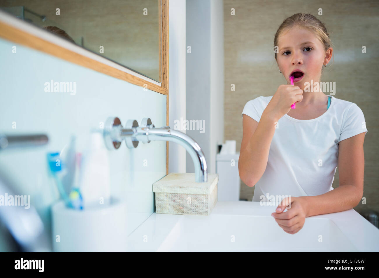 Portrait of girl brushing teeth while standing by sink in bathroom ...