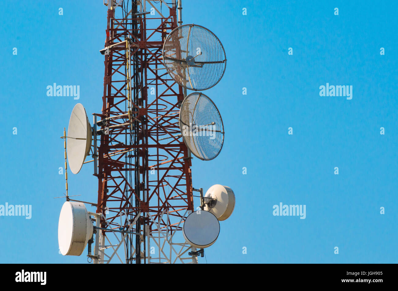 Mobile phone communication antenna tower with satellite dish on blue sky background ...