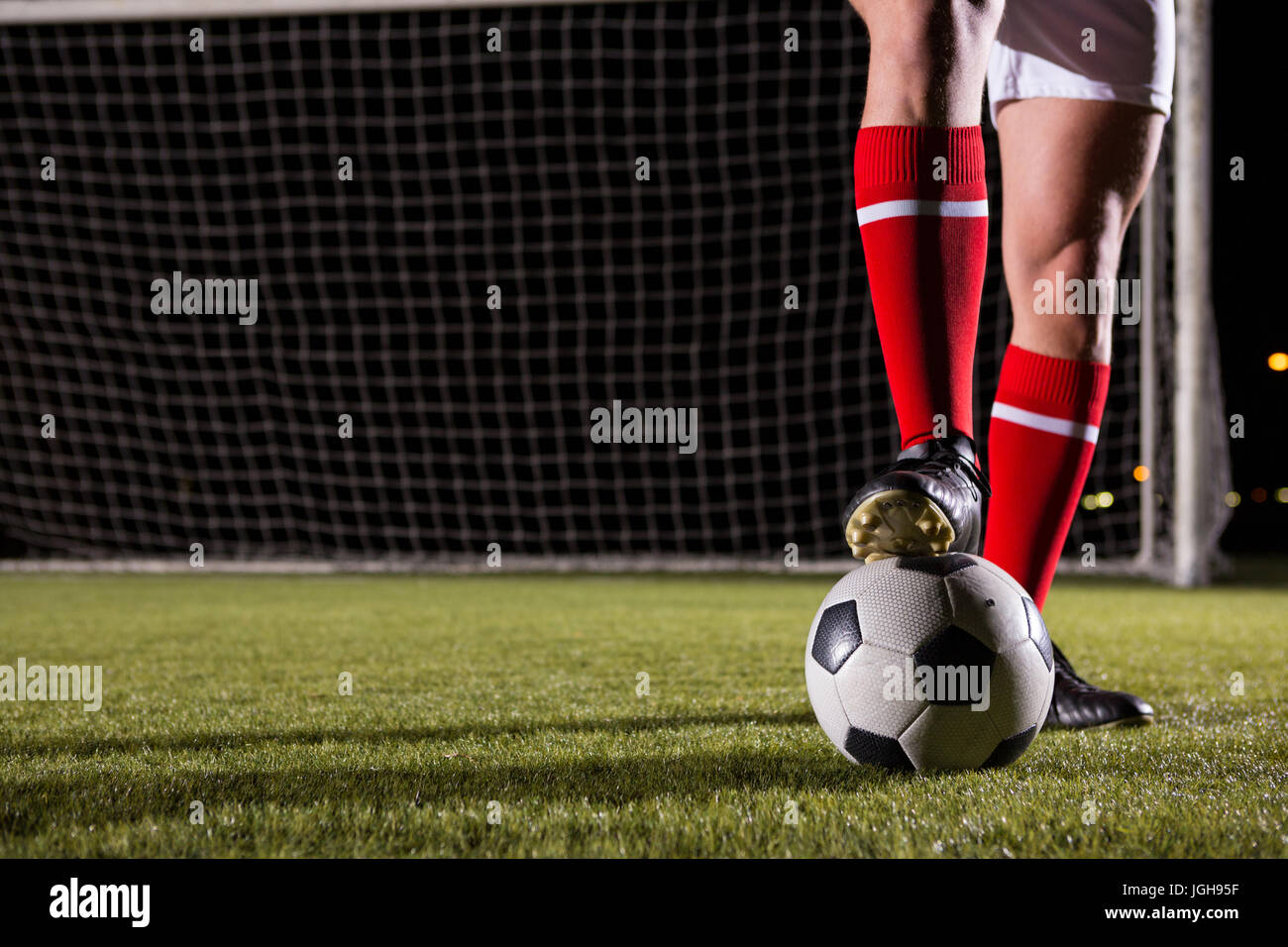 Low section of male soccer player with ball on field against goal post ...