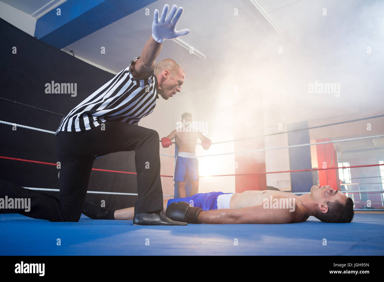 Referee gesturing by unconscious male boxer lying in boxing ring at ...
