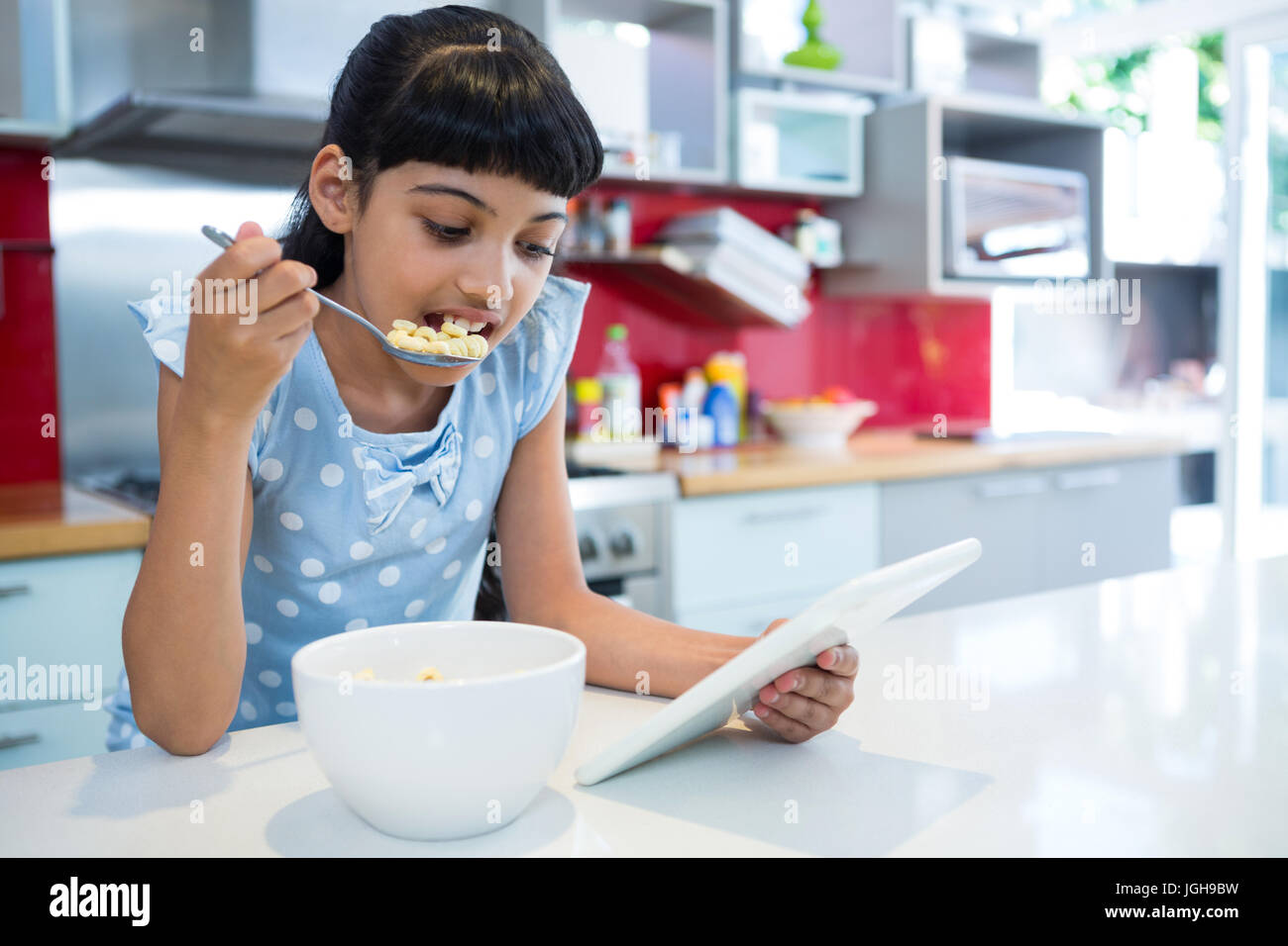 Girl eating breakfast while looking at digital tablet on kitchen ...