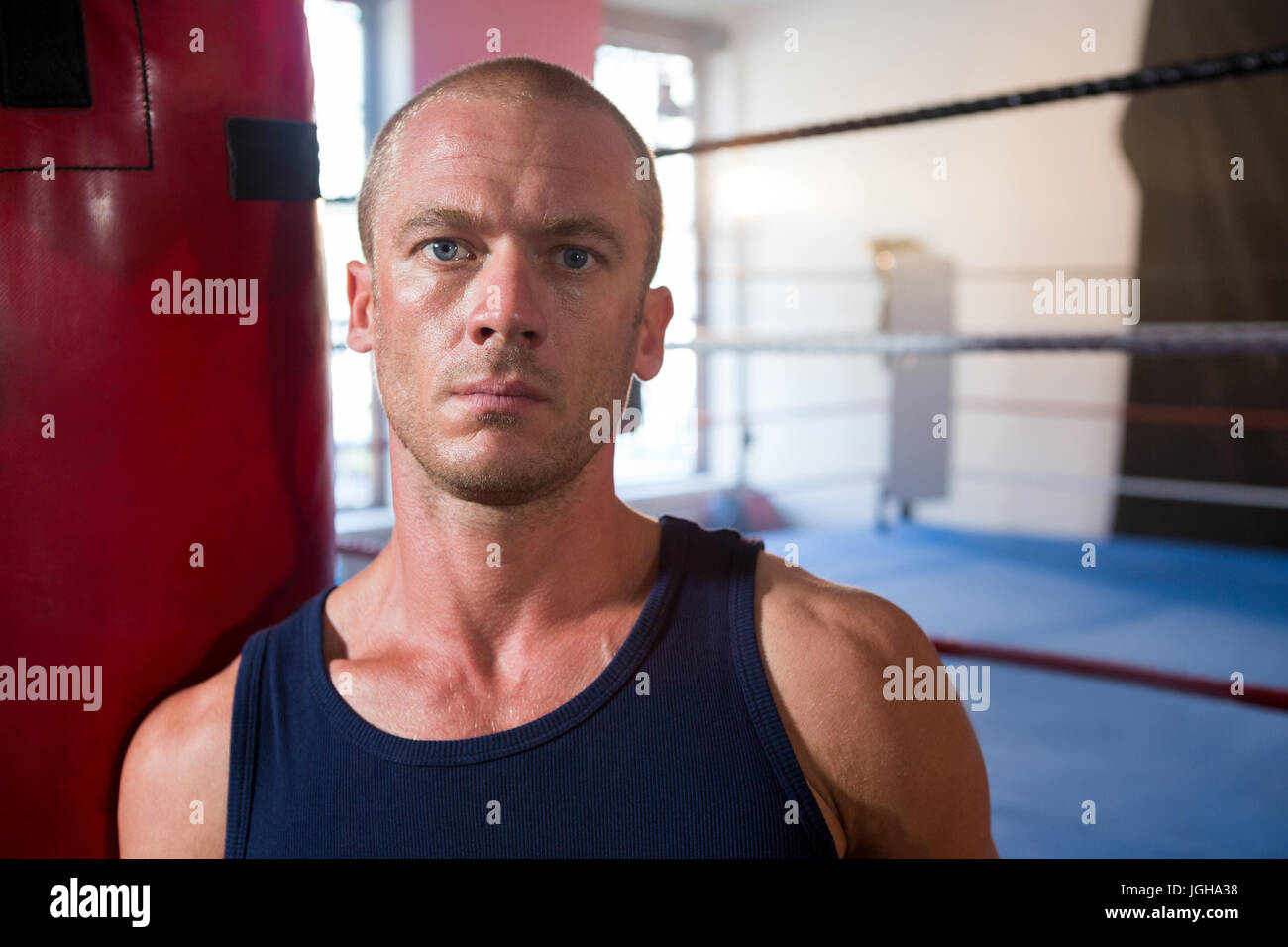 Close-up portrait of young male athlete standing against boxing ring at ...