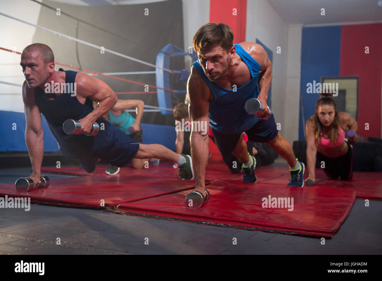 Young athletes exercising with dumbbells by boxing ring at fitness ...