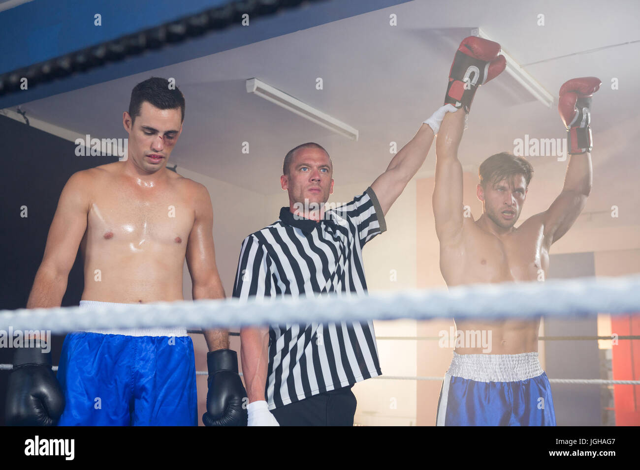 Referee holding hands of winning male boxer by athlete standing in ...
