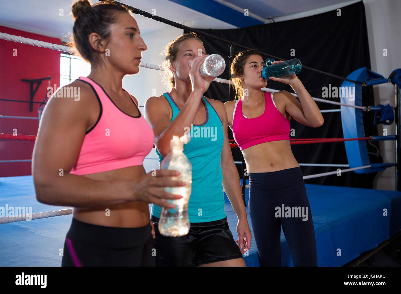 Exhausted young athletes drinking water by boxing ring at fitness ...