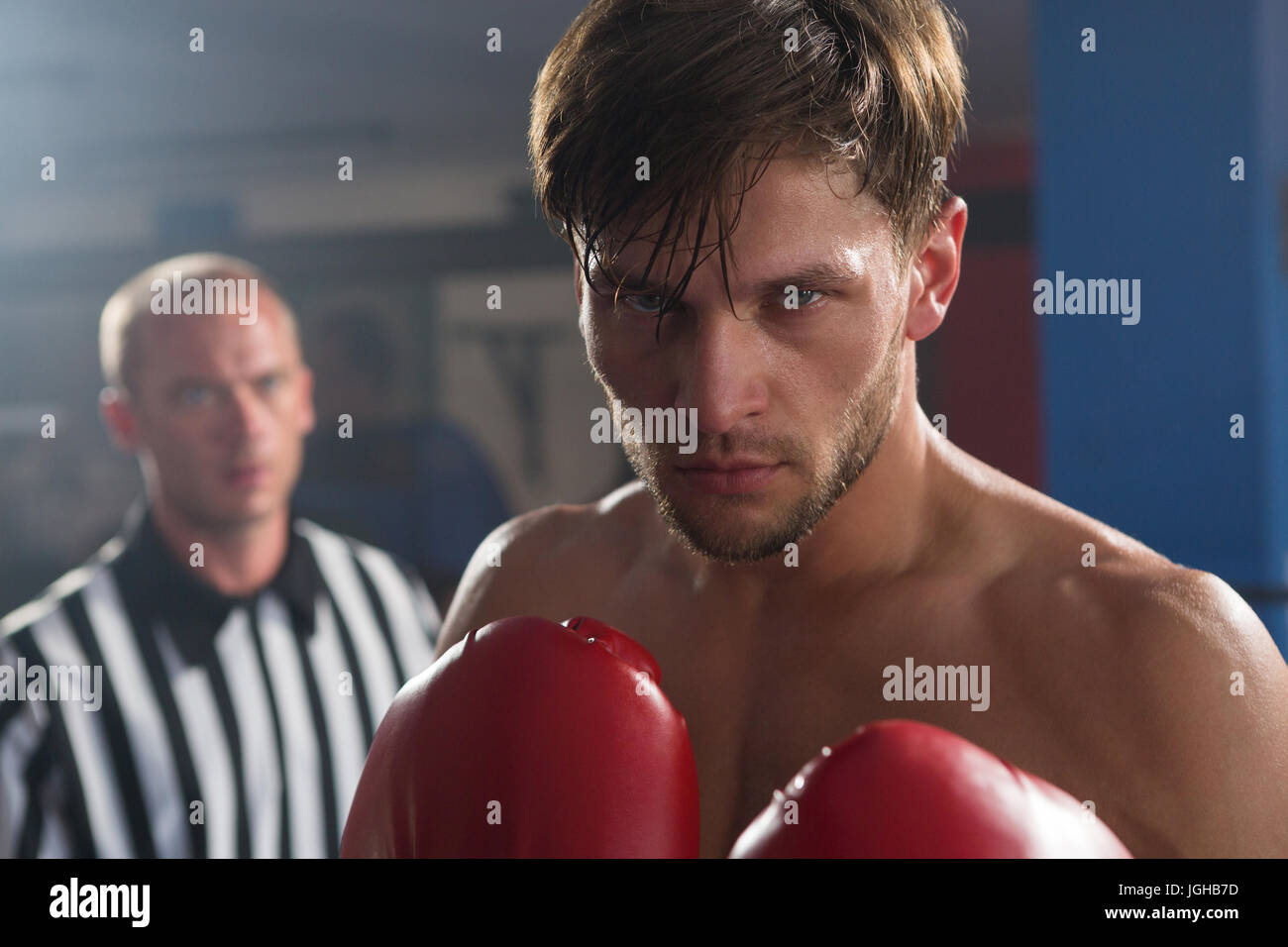 Referee looking at young male boxer in boxing ring at fitness studio ...