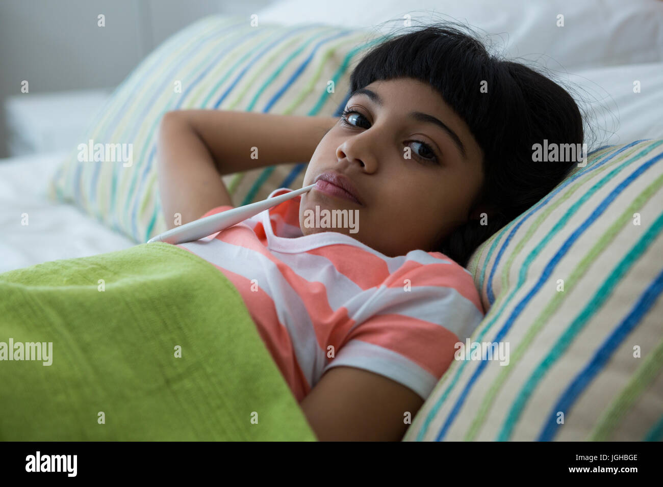 Portrait of sick girl with thermometer in mouth lying on bed at home ...