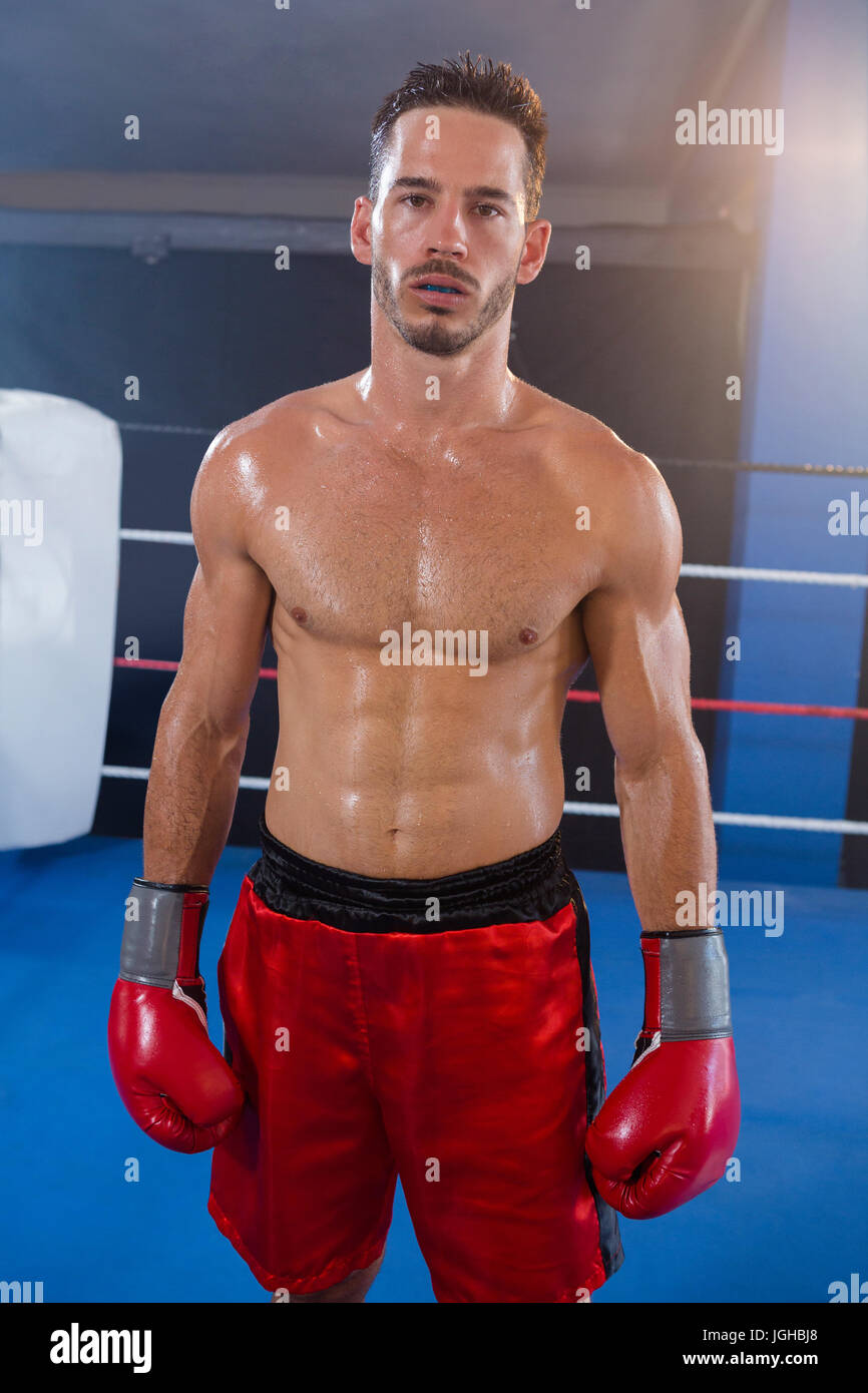 Portrait of confident male boxer wearing red gloves standing in boxing ...