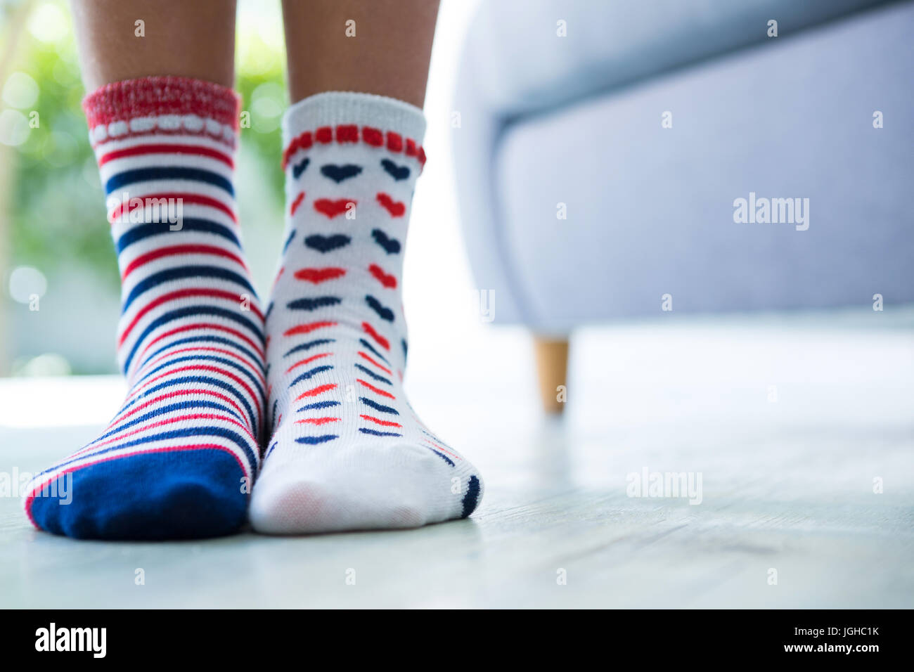 Low section of girl wearing patterned socks while standing at home ...