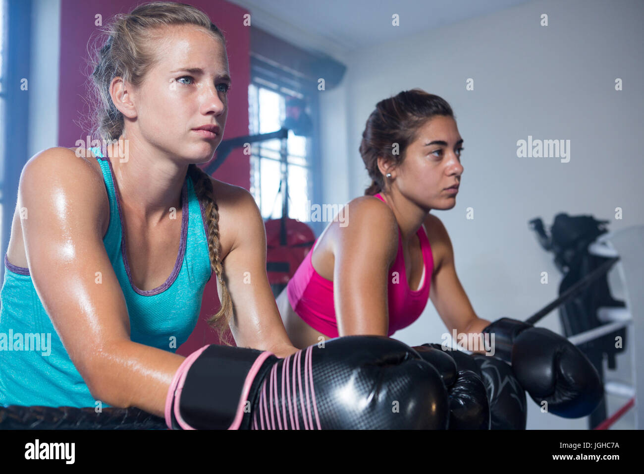 Young female boxers leaning on boxing ring rope while looking away ...