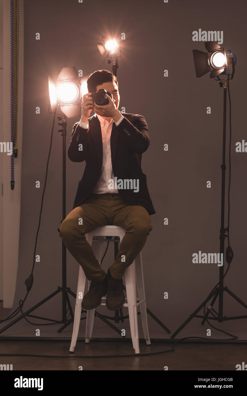 Full length of man photographing while sitting on stool in studio Stock ...
