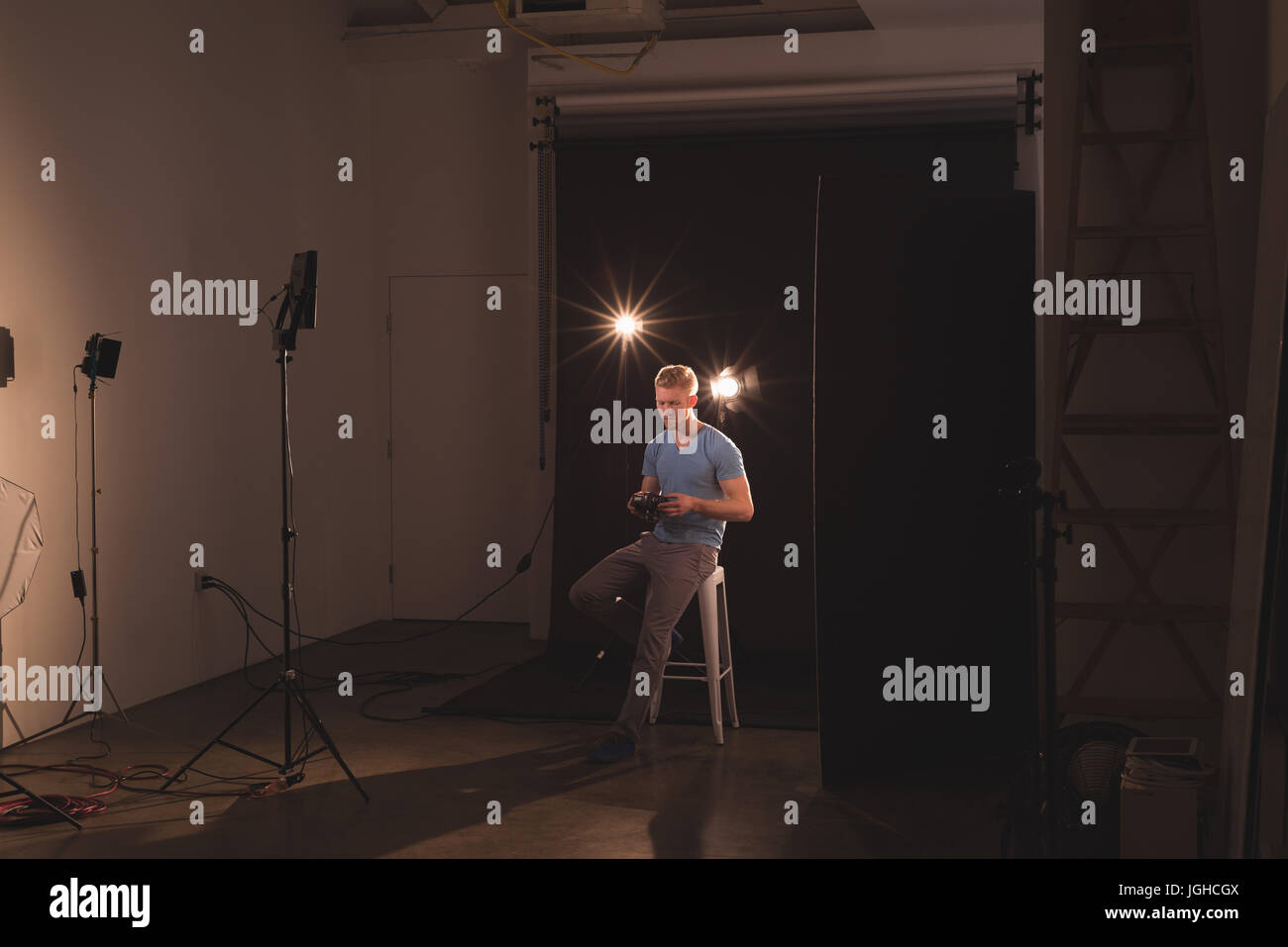 Photographer adjusting camera while sitting on stool against backdrop ...